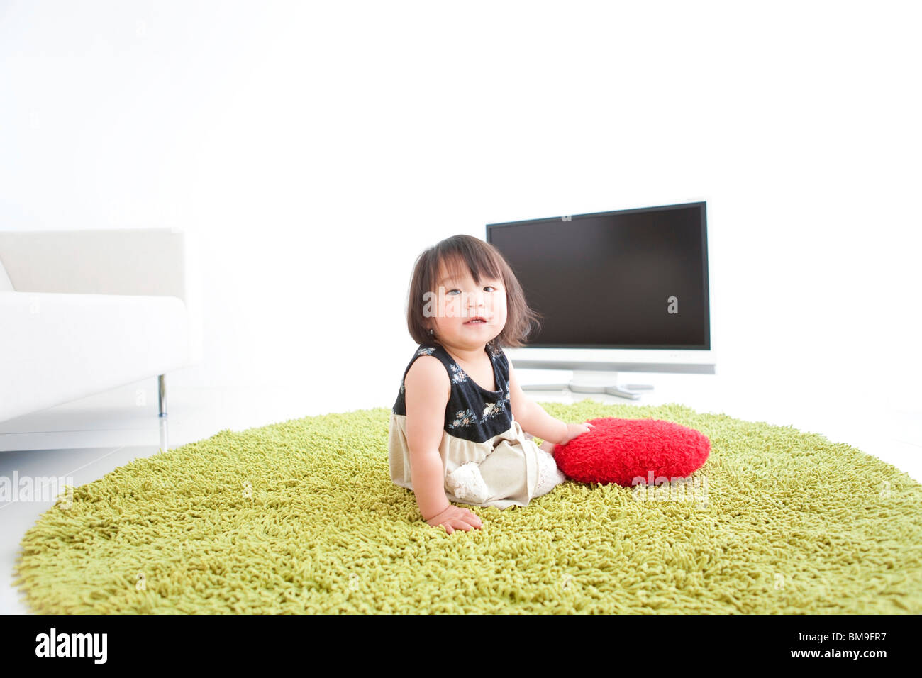 Baby girl sitting on a rug Stock Photo - Alamy