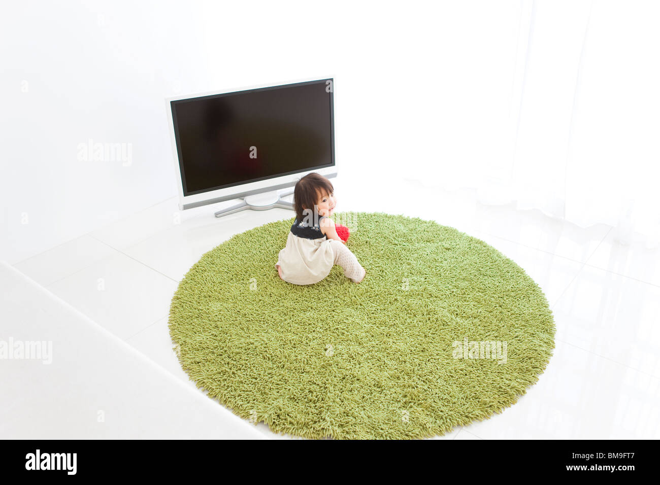Baby girl sitting on rug Stock Photo - Alamy