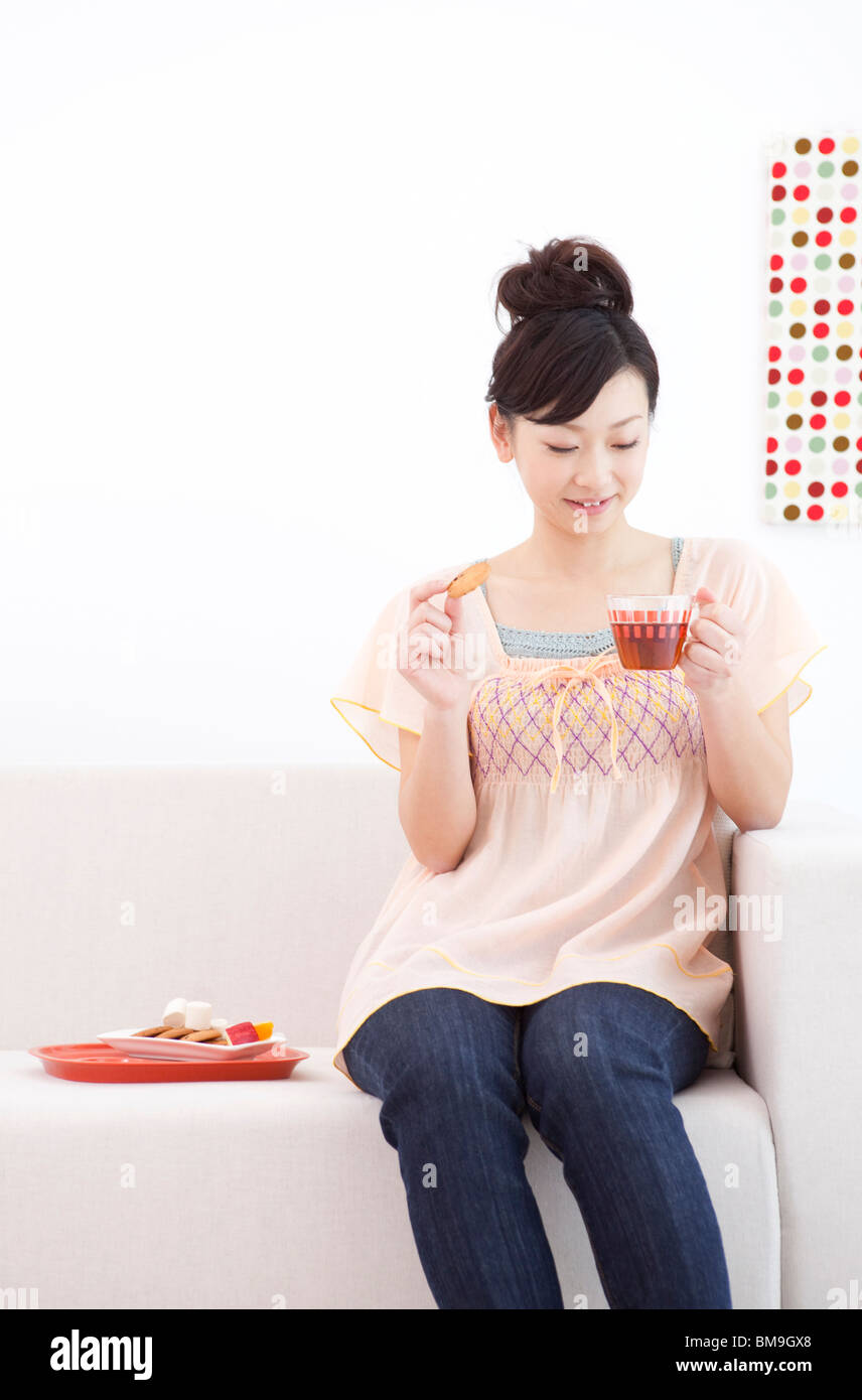 Young woman sitting on couch drinking tea Stock Photo - Alamy