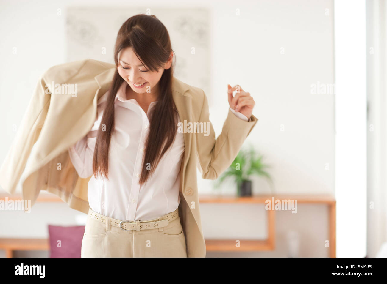 Young woman putting on jacket, smiling Stock Photo - Alamy