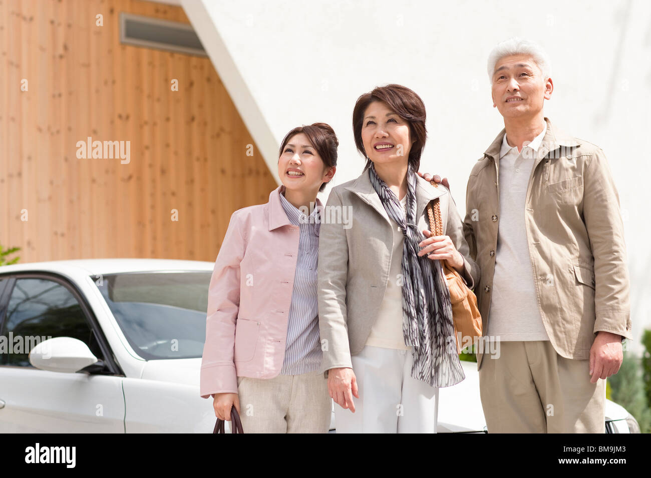 Young woman with parents standing by car, smiling and looking away ...