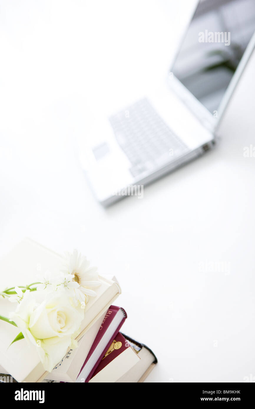 White flowers on piled book, laptop in background, white background ...