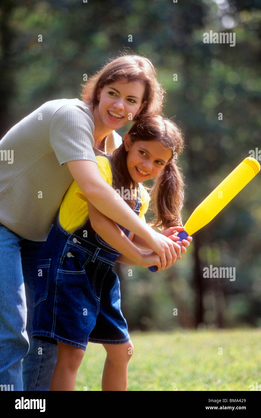 Woman shows her daughter how to use a bat in baseball Stock Photo - Alamy