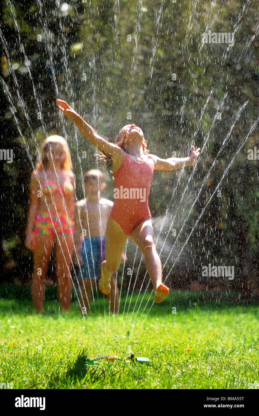 Girl jumping through lawn sprinkler Stock Photo - Alamy