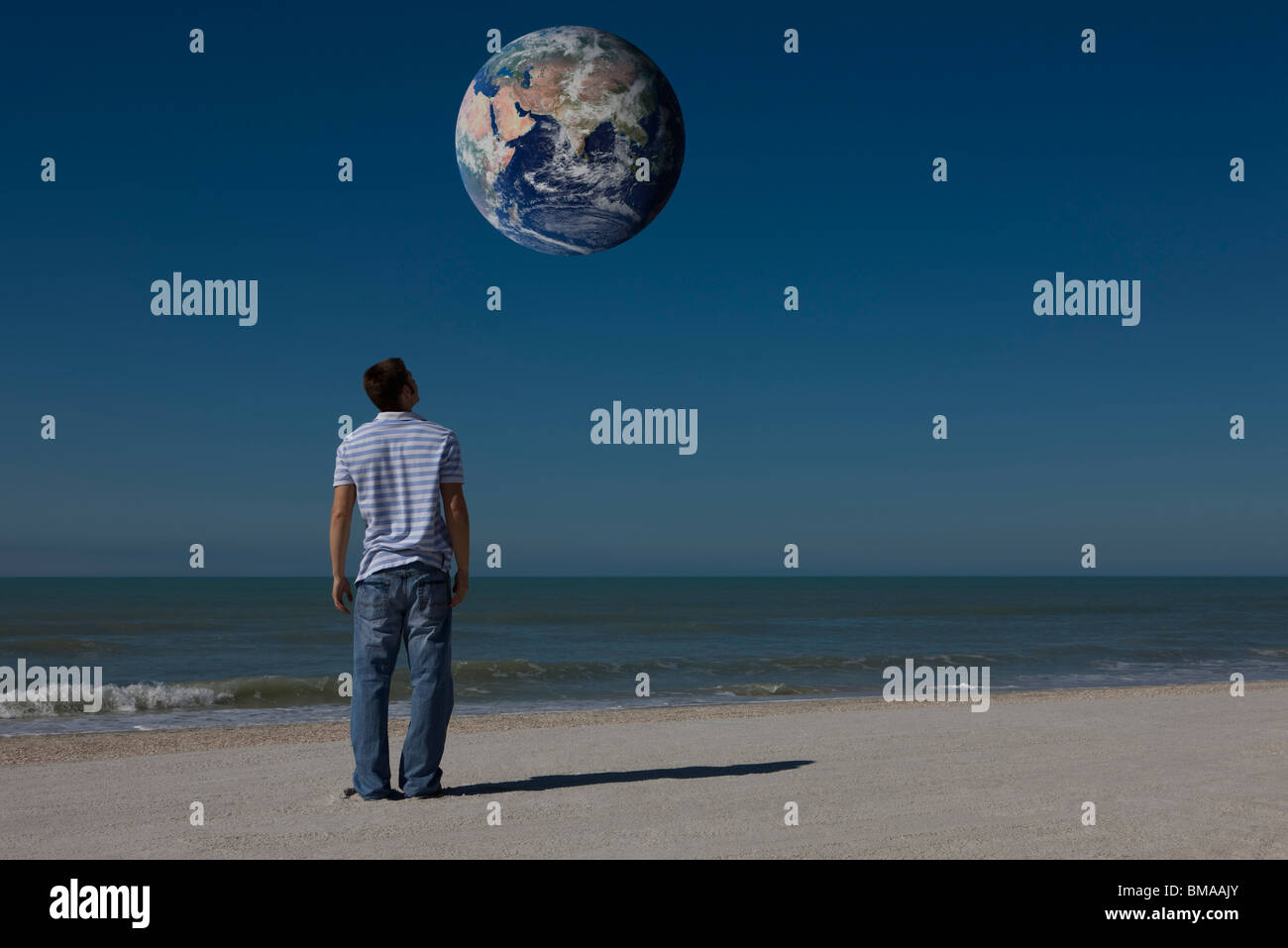 Man on beach looking up at planet earth orbiting overhead Stock Photo ...