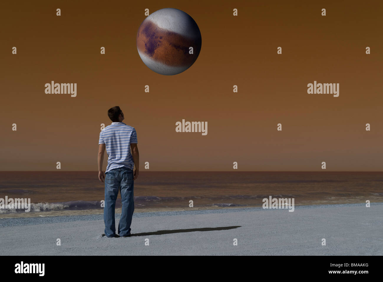 Man on beach looking up at alien world orbiting overhead against brown ...