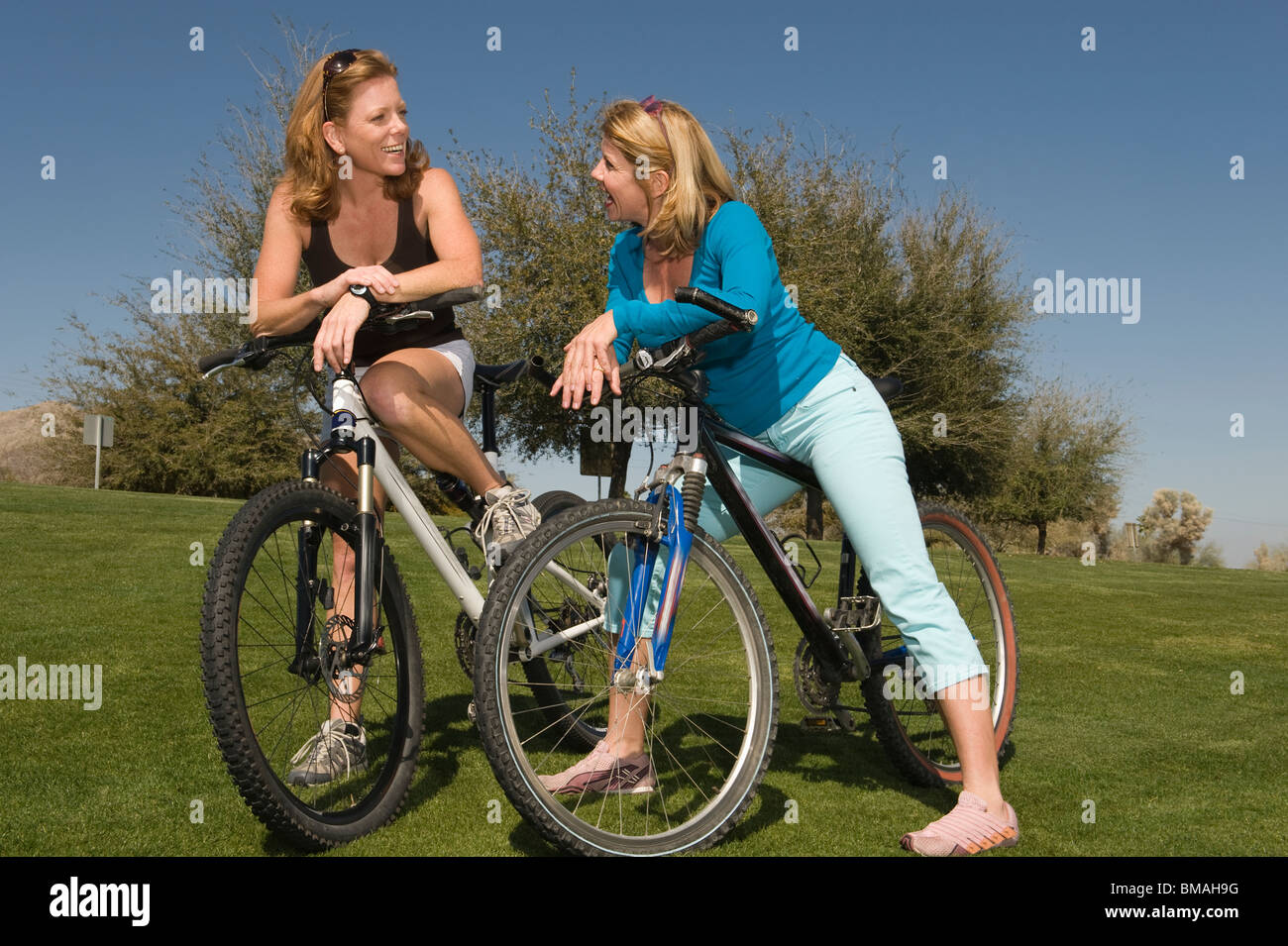 Two friends lean on their bikes talking Stock Photo - Alamy