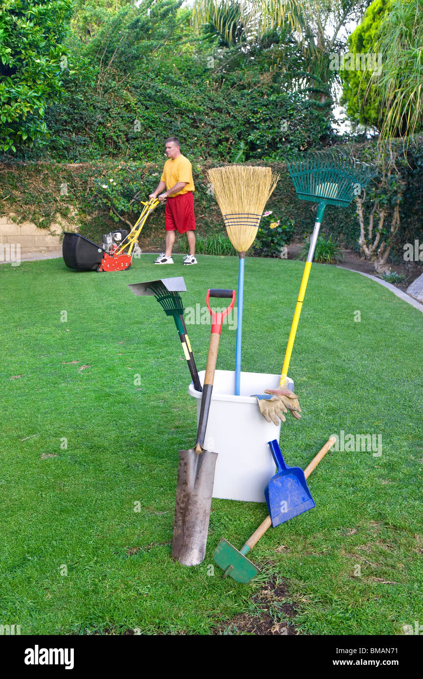 A Gardner mows a lawn and prepares to conduct other gardening work ...