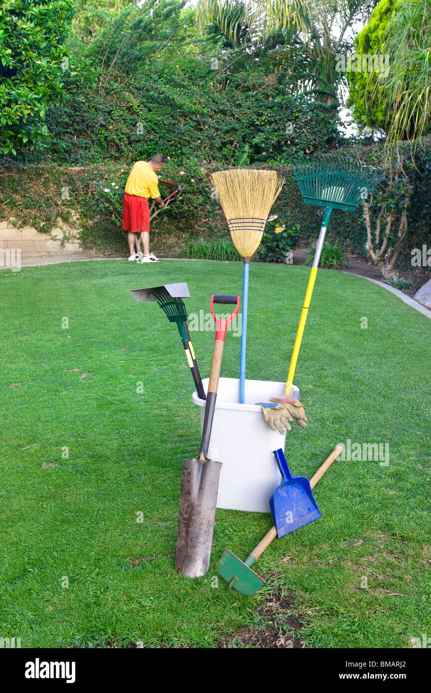 A man works in his yard trimming shrubbery and conducting lawn care ...