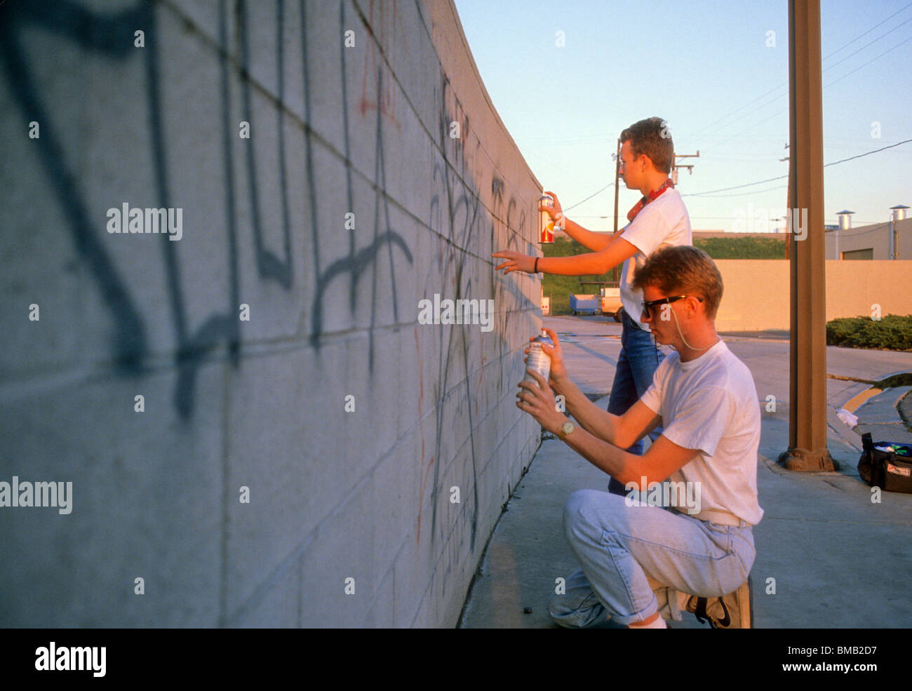 Two white teen male boy spray graffiti on wall mar destroy damage ...