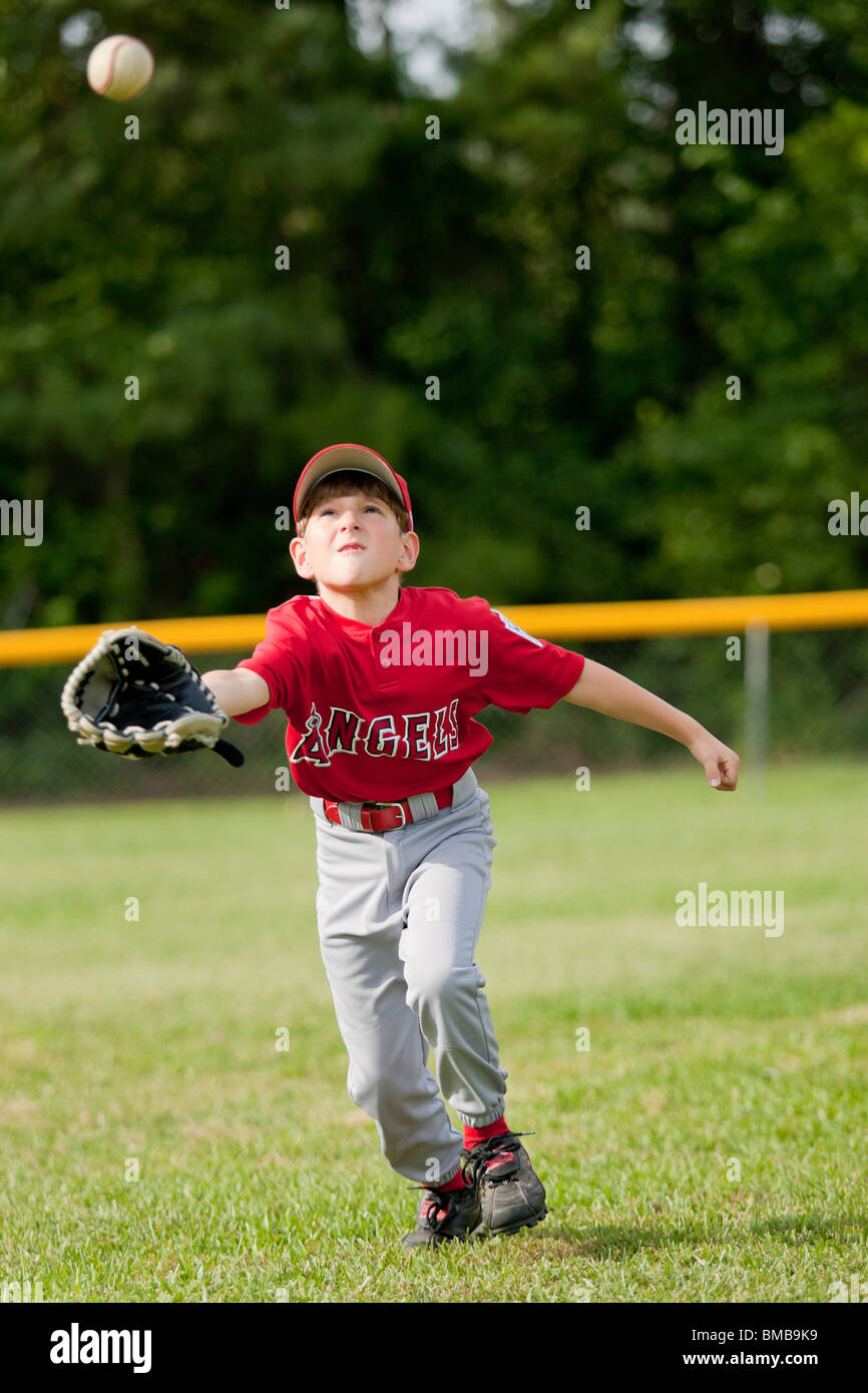 young boy wearing a red "Angels" uniform about to catch a baseball ...