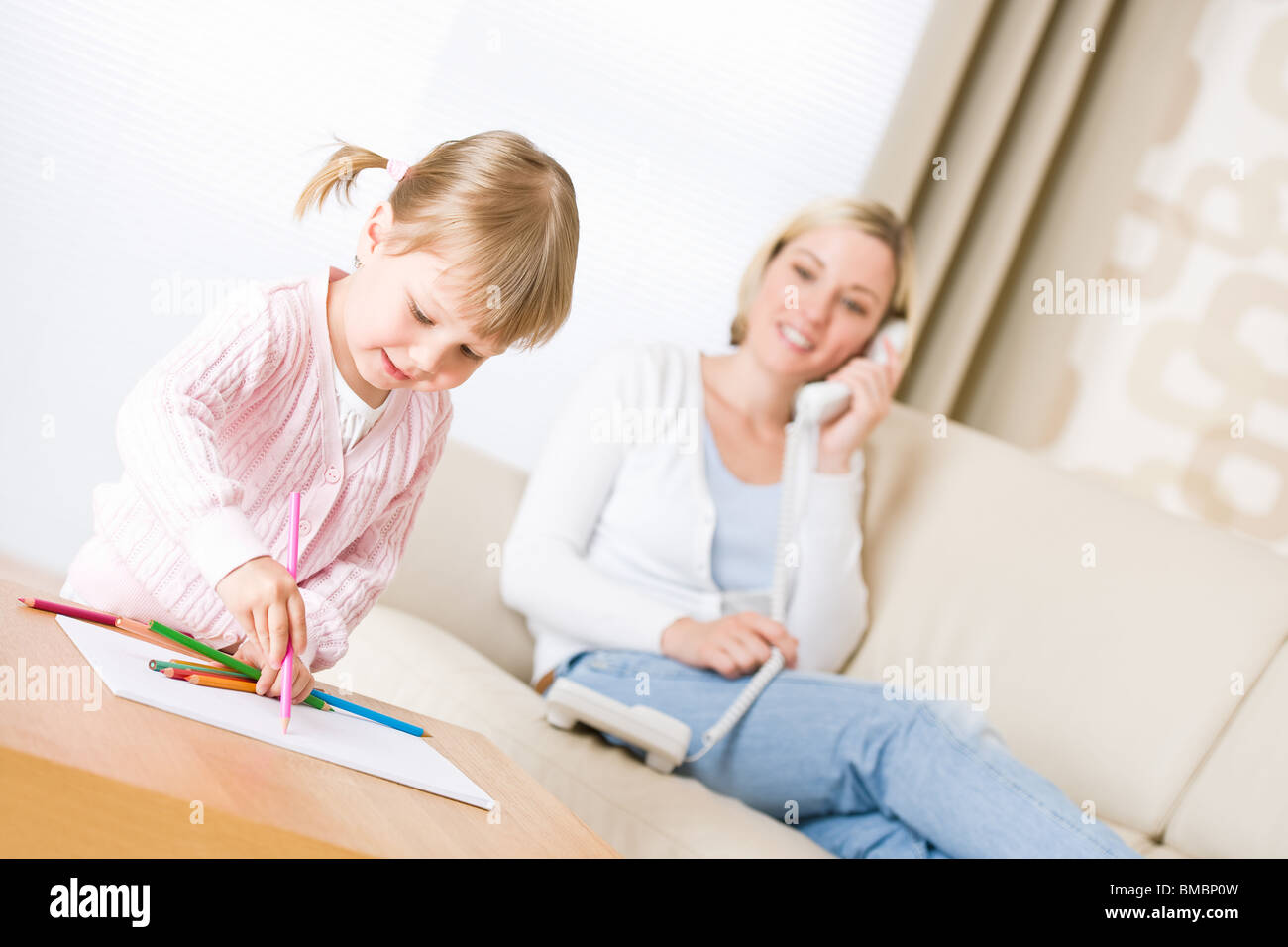 Little girl draw with color pencil in lounge, mother with phone calling ...