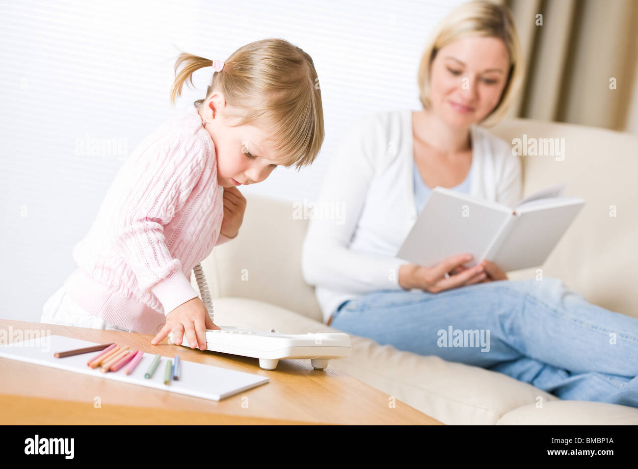 Little girl dial number on phone in living room, mother in background ...