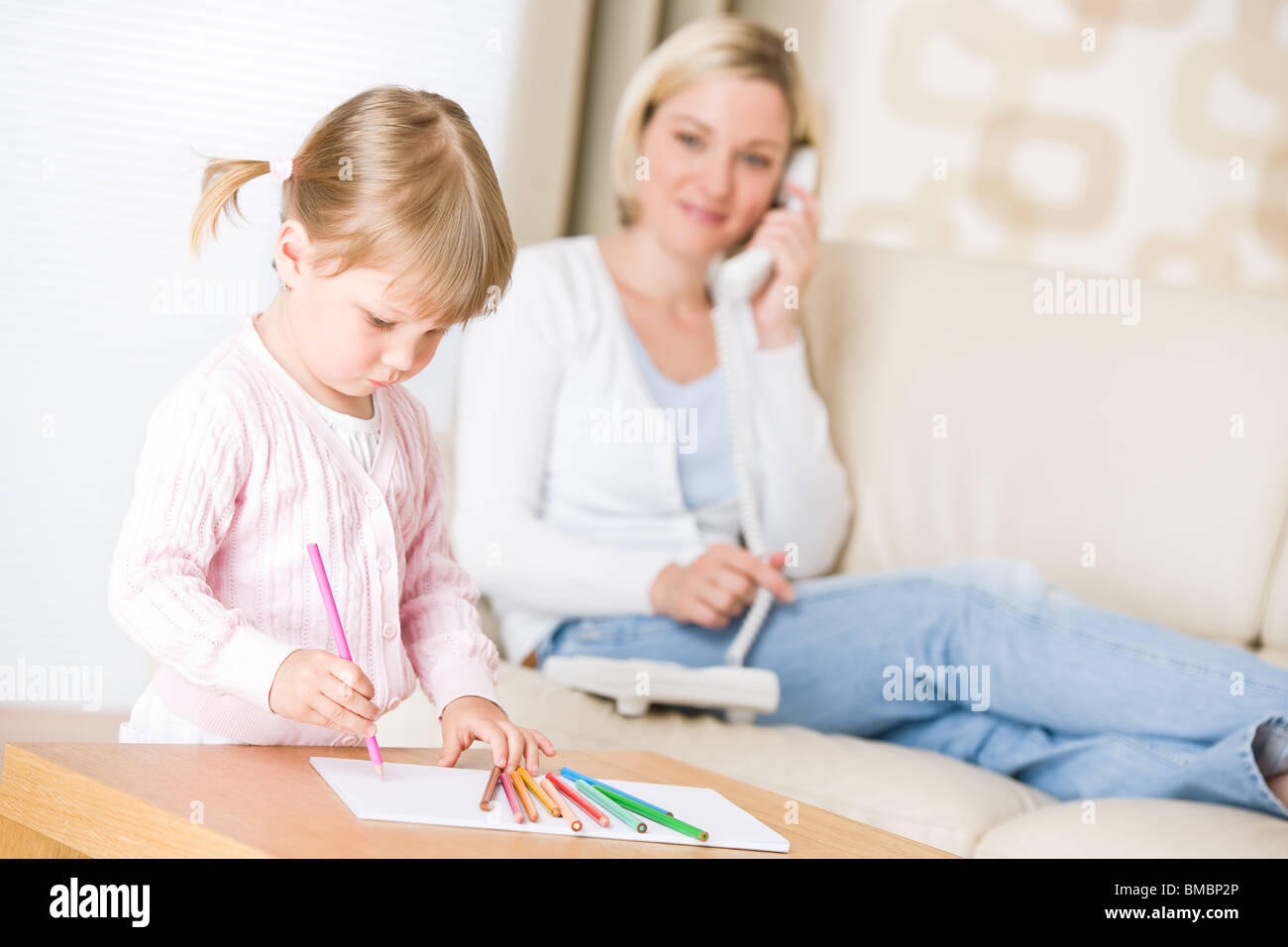 Little girl draw with color pencil in lounge, mother with phone calling ...