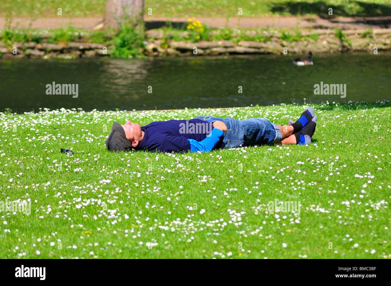 Man sleeping on grassy bank of river in Park Stock Photo - Alamy