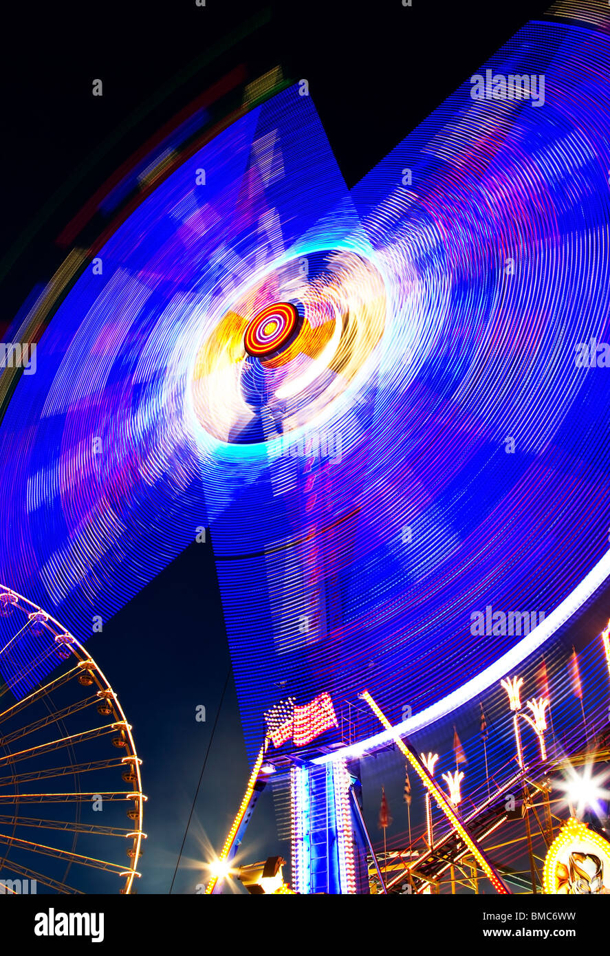 fast merry-go-round by night with great lights and ferris wheel in ...