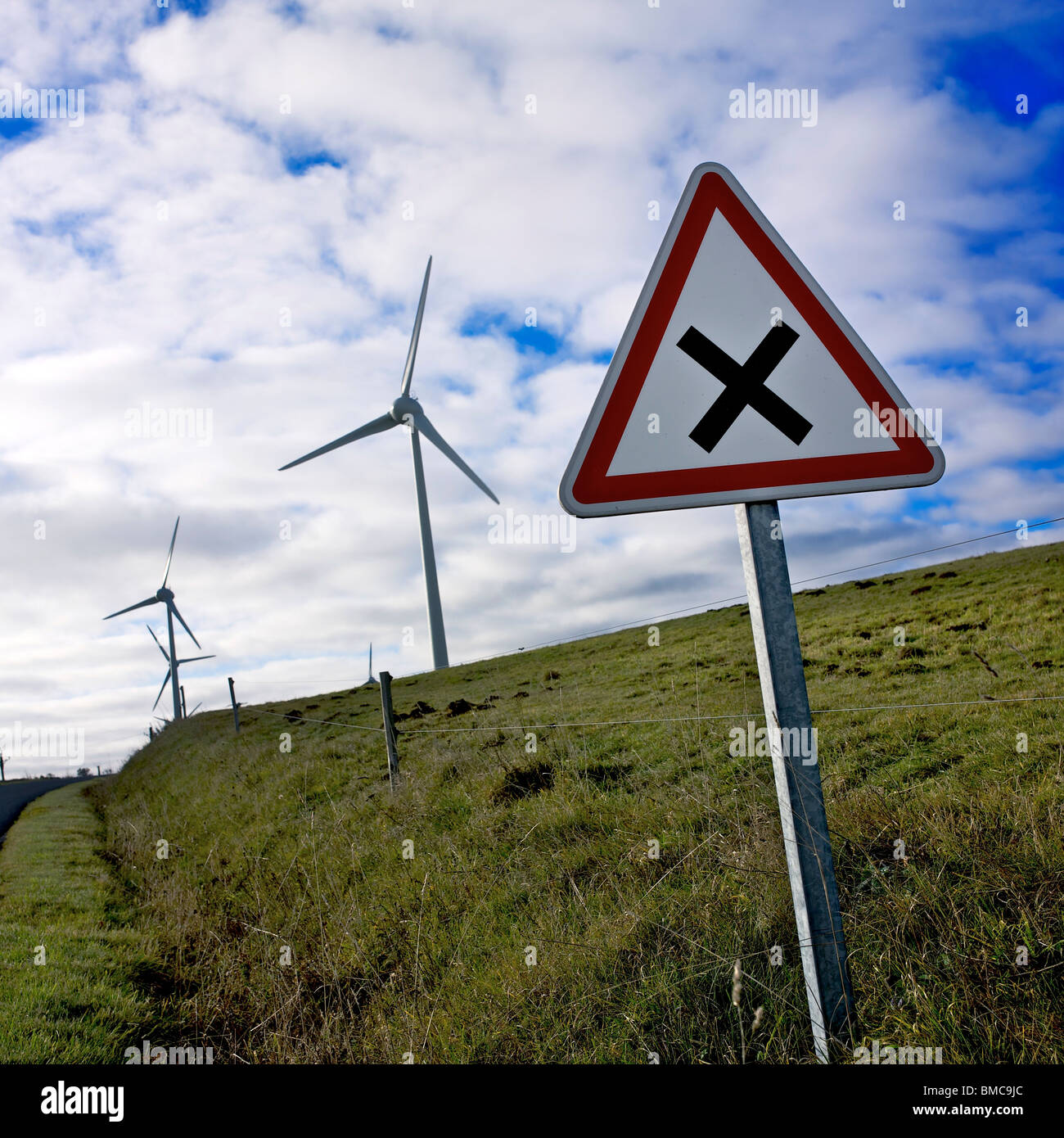 Warning sign in front of wind turbines on a grassy hillside under a ...