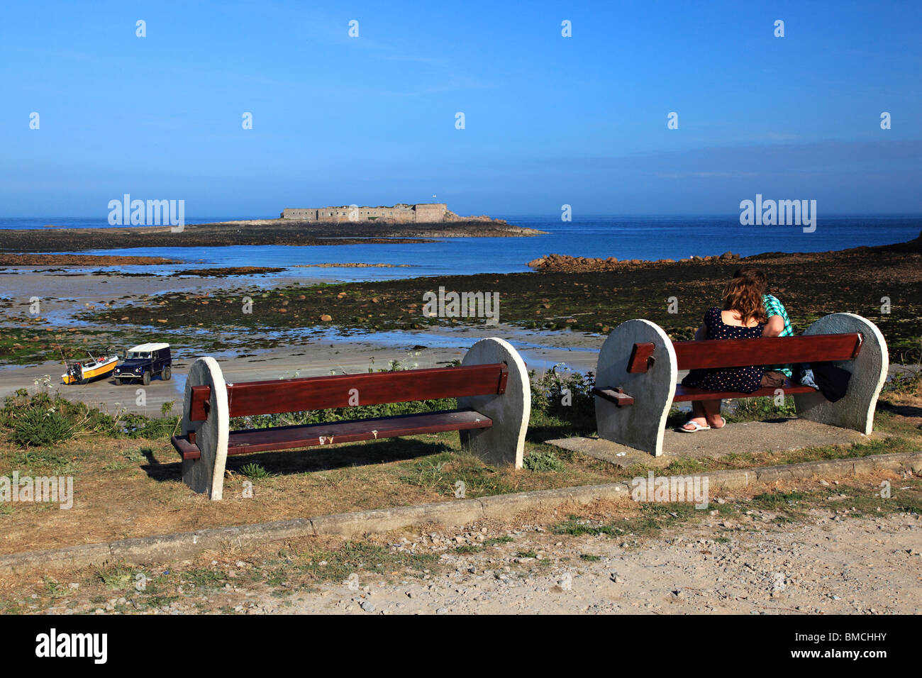 Young couple sitting on the bench in Longis Bay overlooking Ile de Raz ...