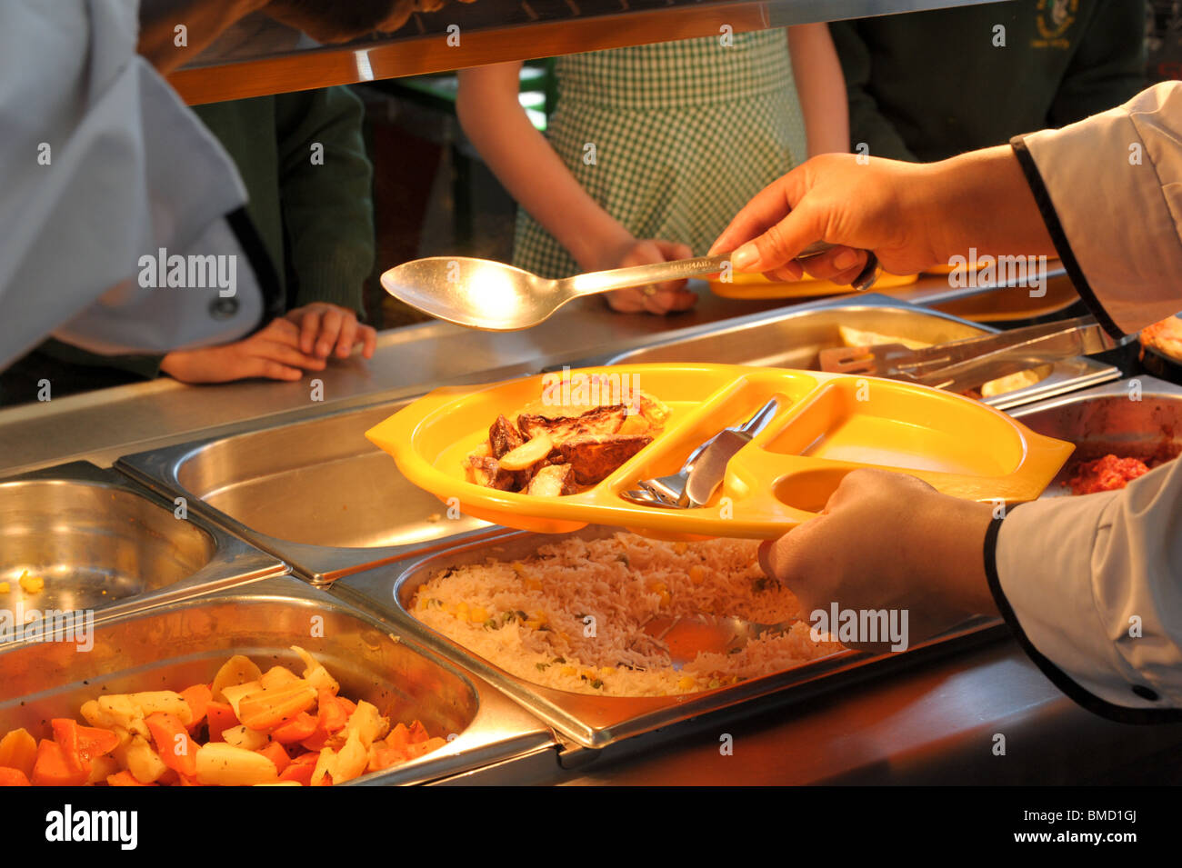 Dinner lady serves up school meals on a yellow plastic tray to primary ...