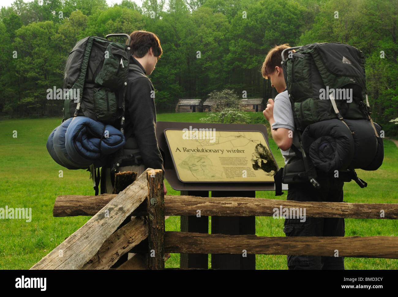 Hikers reading the sign in front of log cabin replicas from the ...