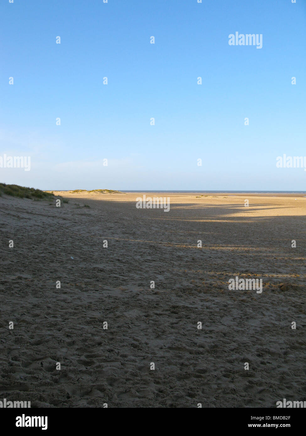 A sandy beach in shadow. A blue sky and strip of yellow sand can be ...