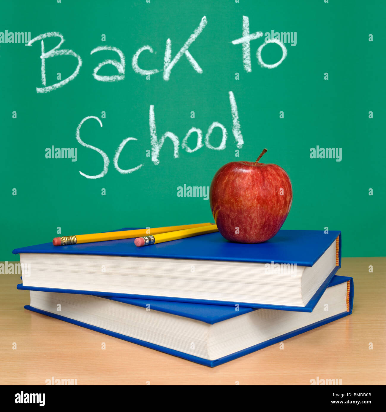 Back to school written on a chalkboard. Books, pencils and an apple on ...