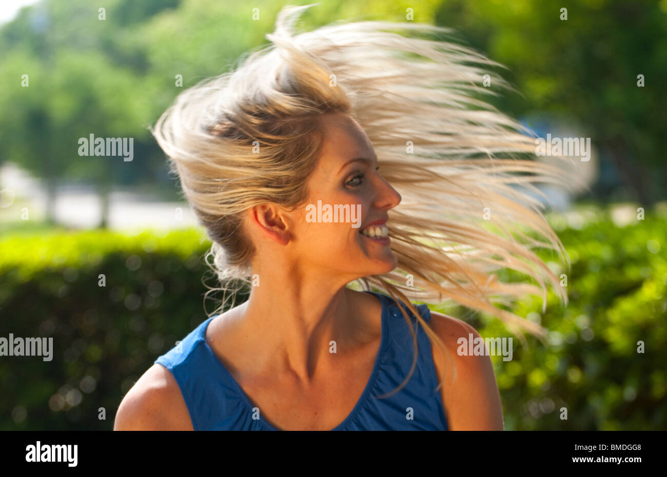 Beautiful portrait of blonde woman outdoors in sunshine spinning hair ...