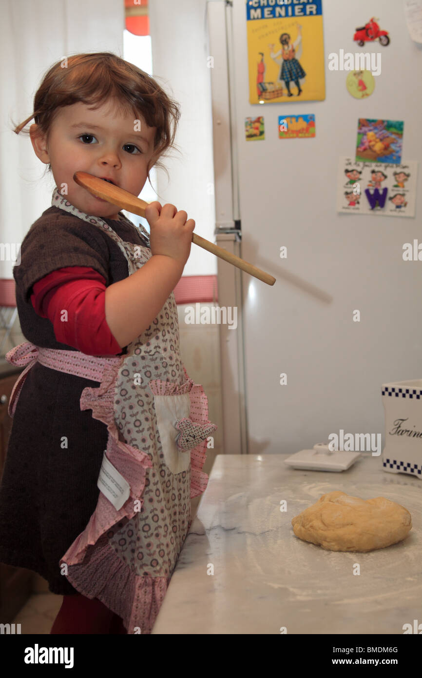 24 month old girl licking spoon and kneading dough for pizza in the ...
