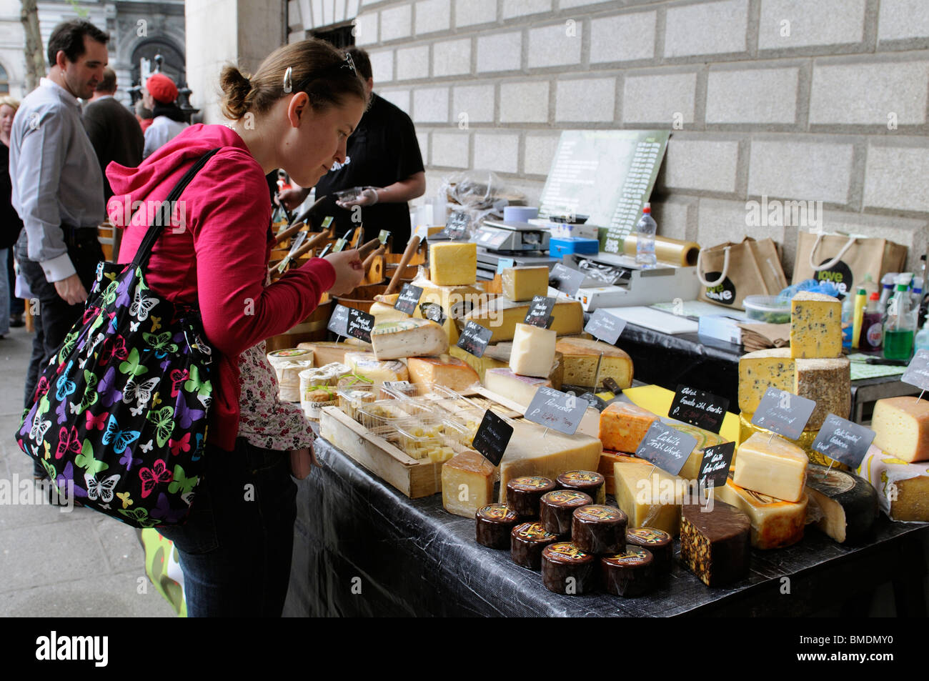 Young woman selecting cheeses from a farmers market cheese stall out ...