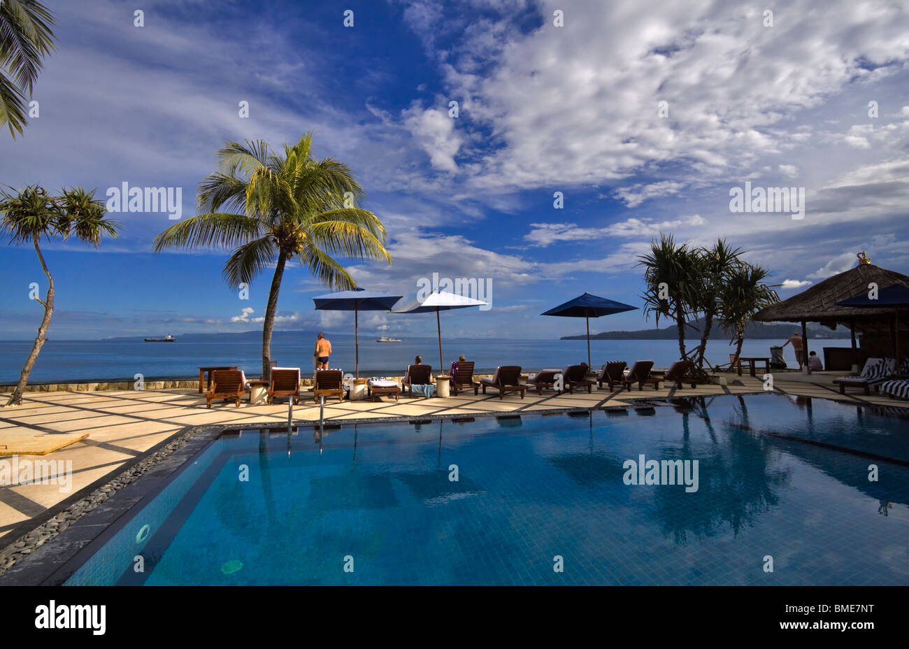 Guests relax by a hotel pool in Bali, Indonesia. View across Badung ...