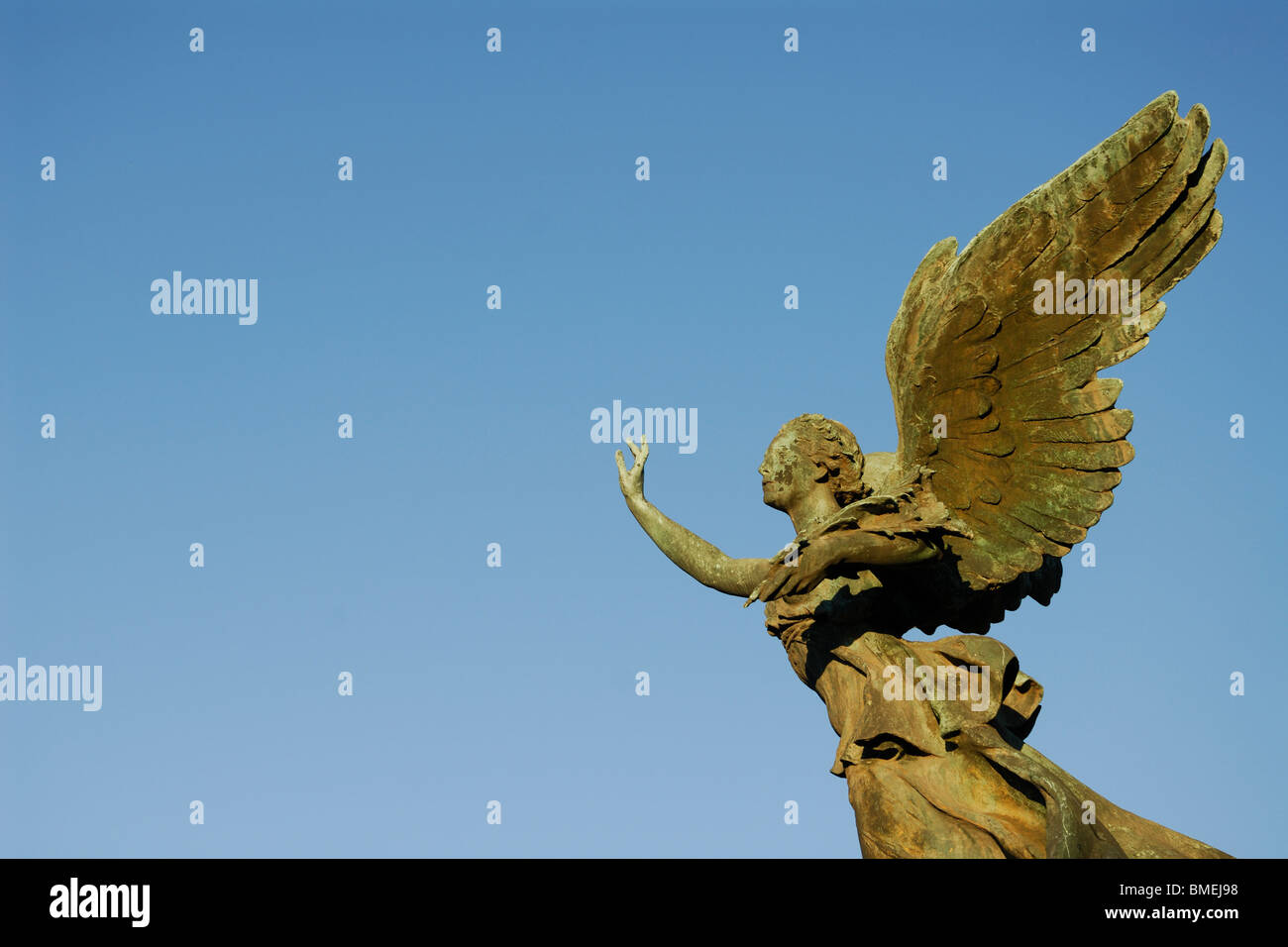 Statue of a winged angel against a plain blue sky background Stock ...
