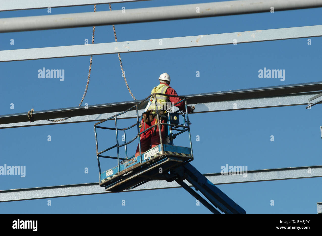 Construction worker working on a cherry picker fitting a roof on a new ...