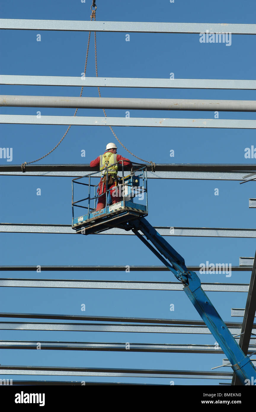 Construction worker working on a cherry picker fitting a roof on a new ...