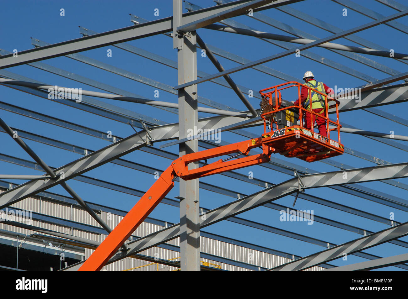 Construction worker working on a cherry picker fitting a roof on new ...