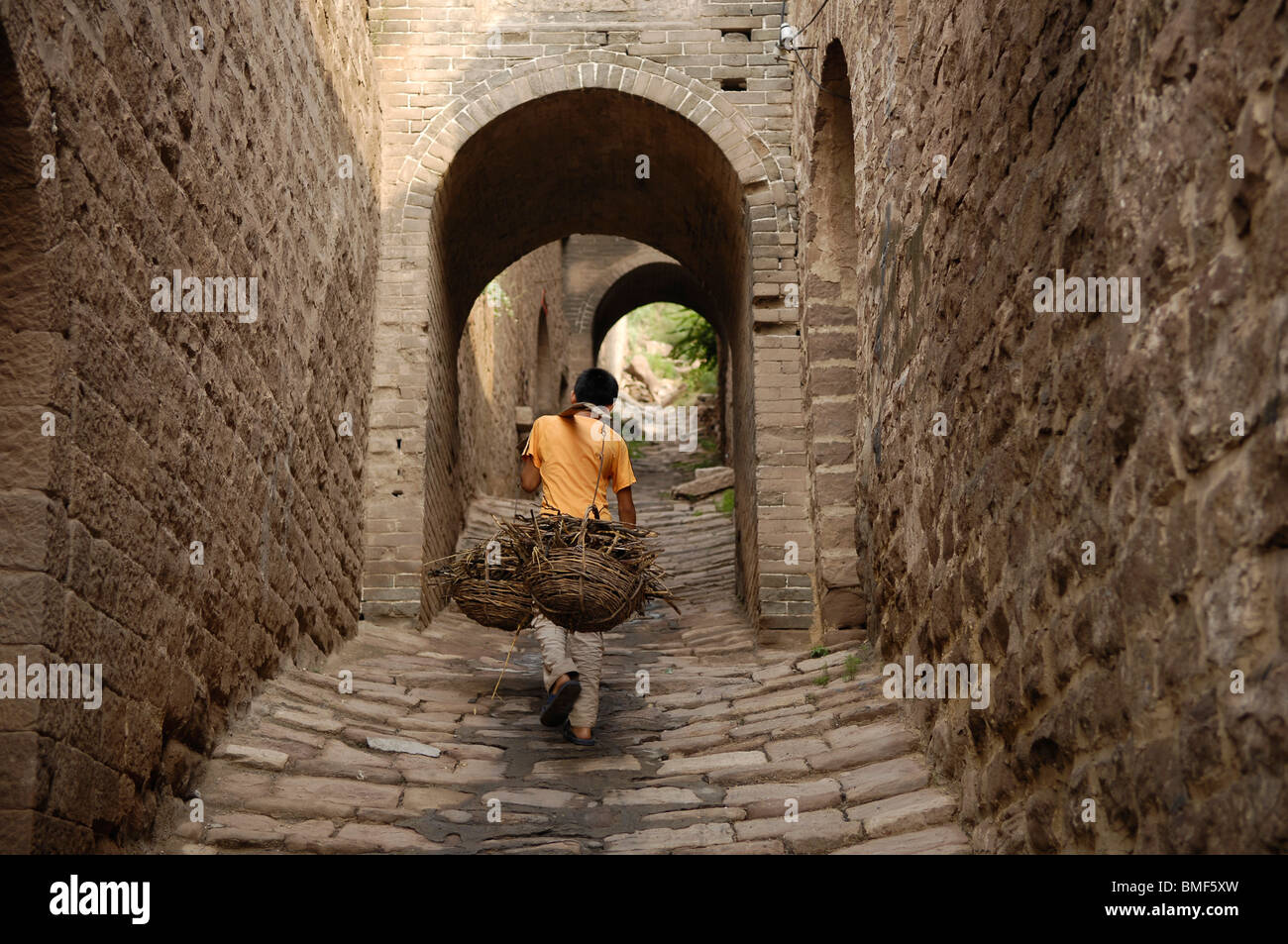 Man walking in narrow alley with baskets of firewood, Qikou, Luliang ...