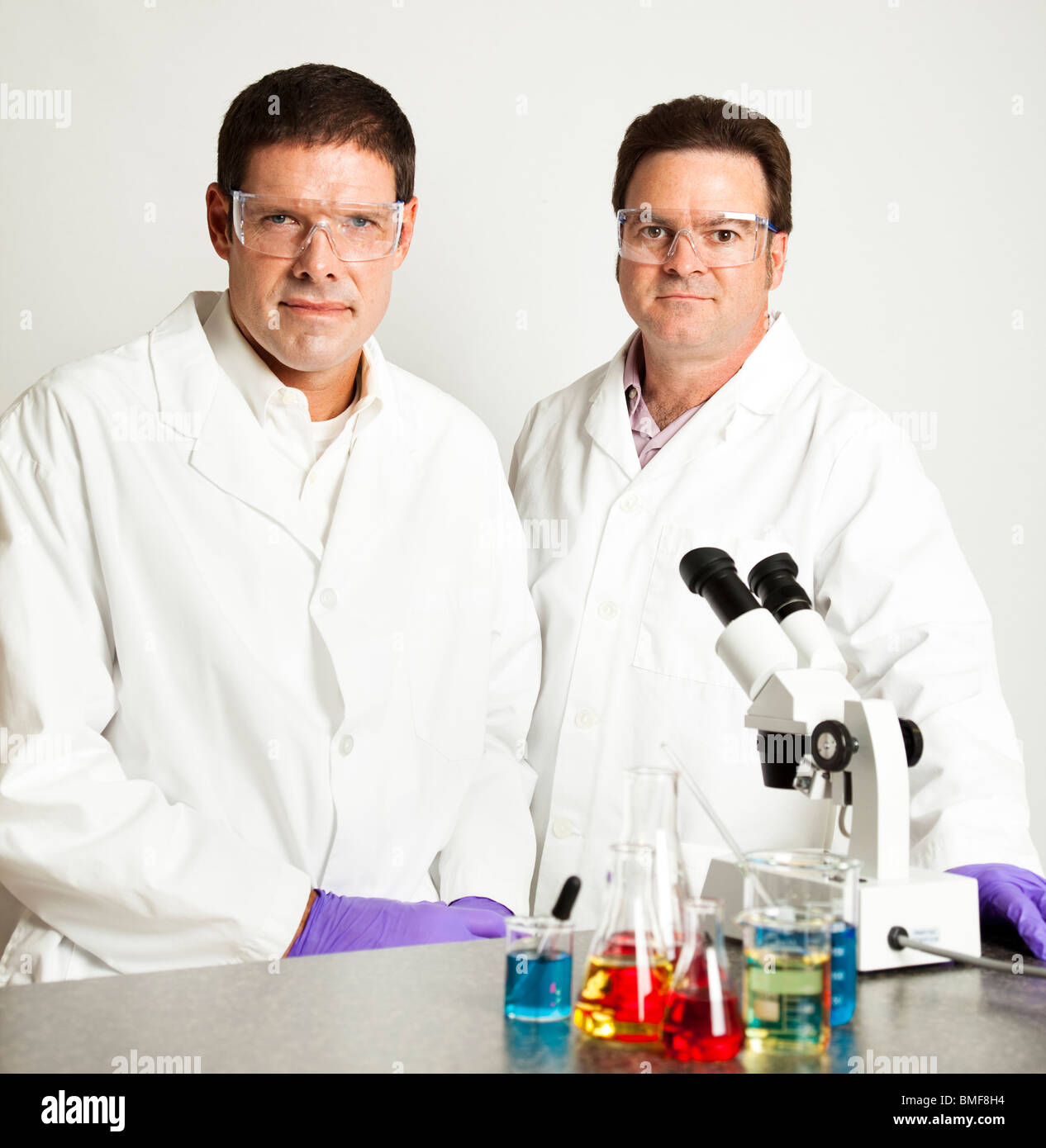 Two male scientists in their laboratory, with microscope and beakers of ...
