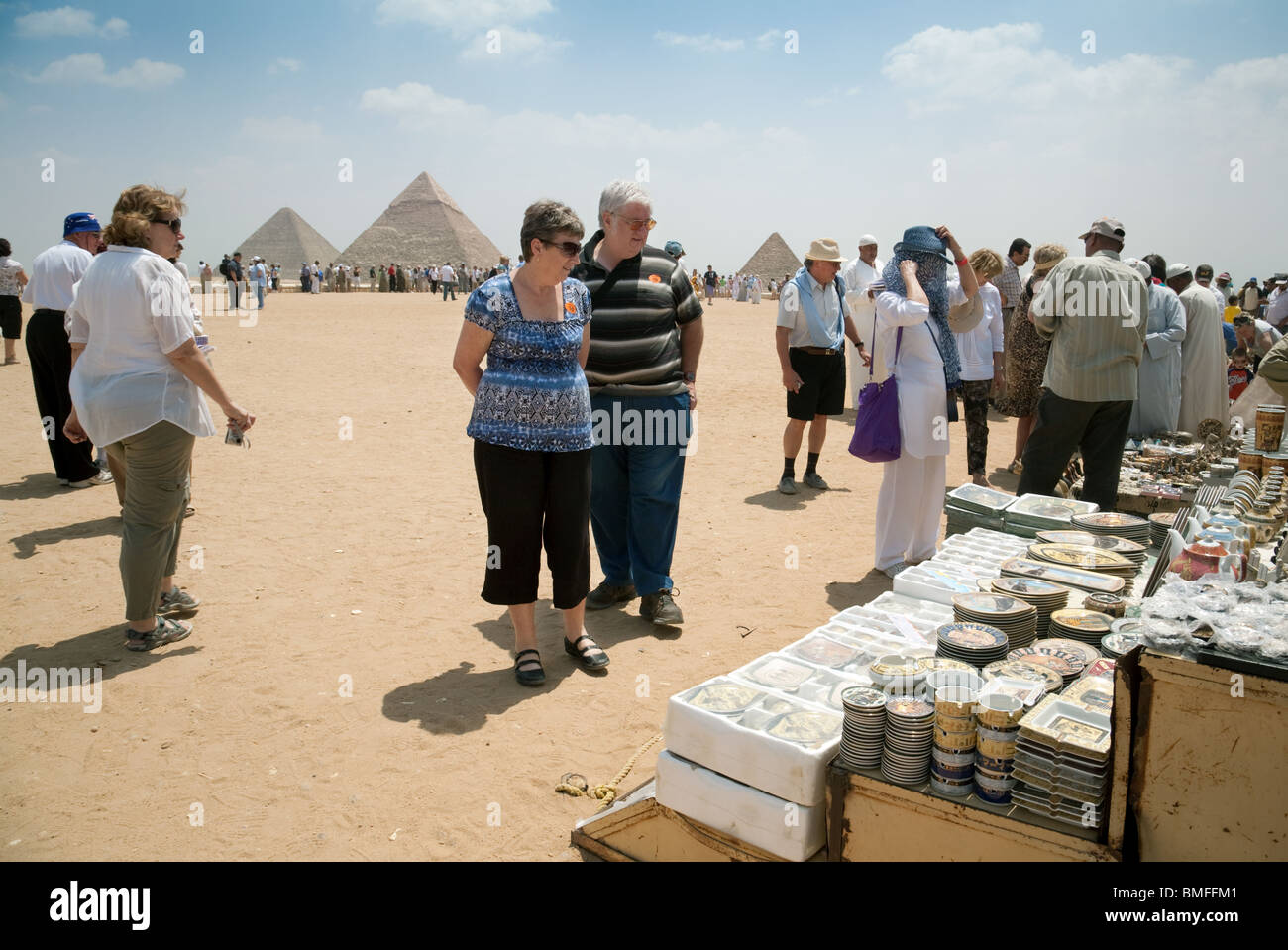 Tourists looking at market stalls with the pyramids in the background ...