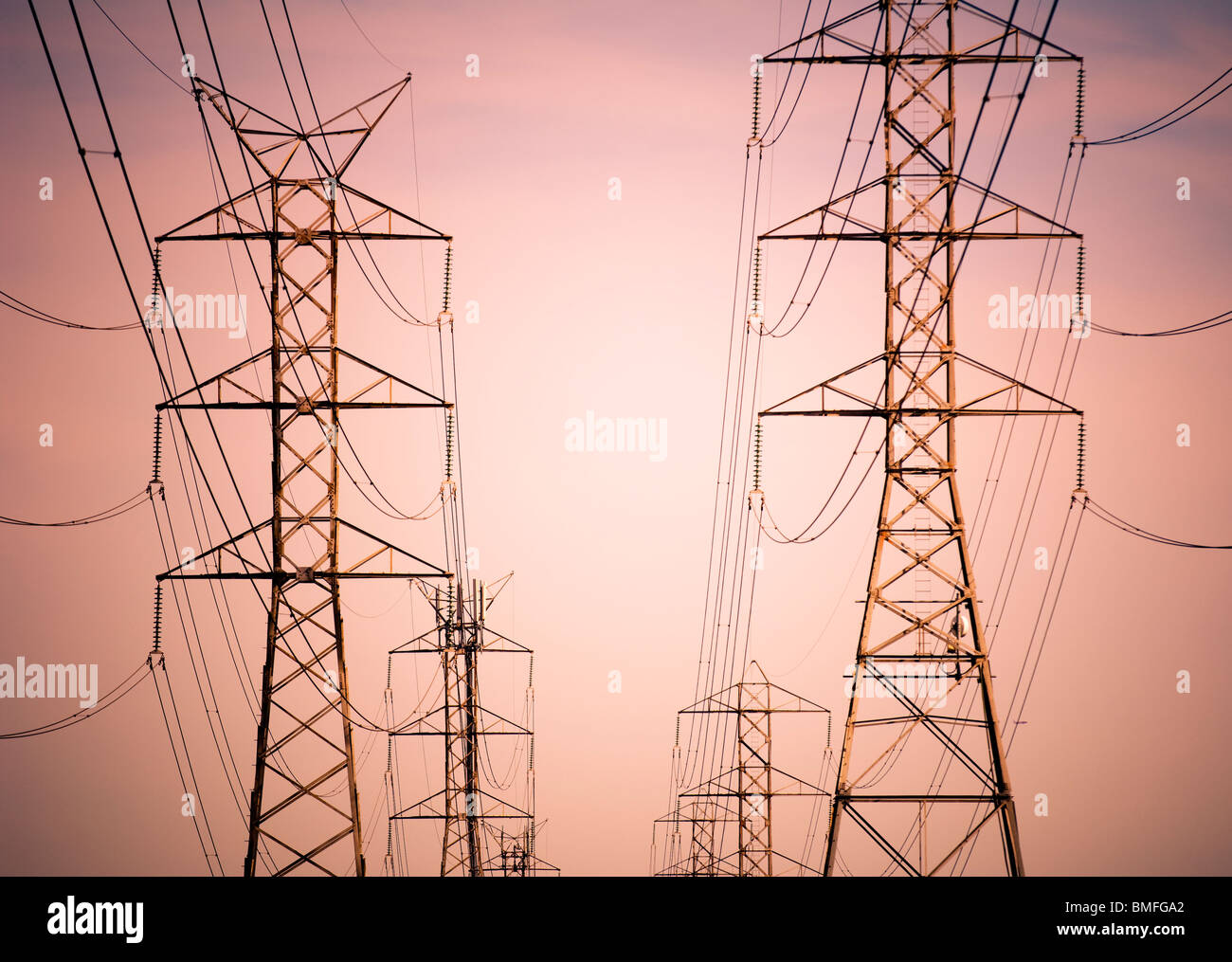 Massive power lines stretch into the distance against a pink sunset sky ...