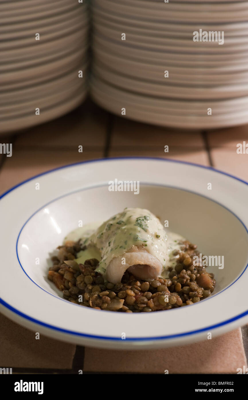 A bowl of lentils topped with baked fish in a creamy herb sauce served ...