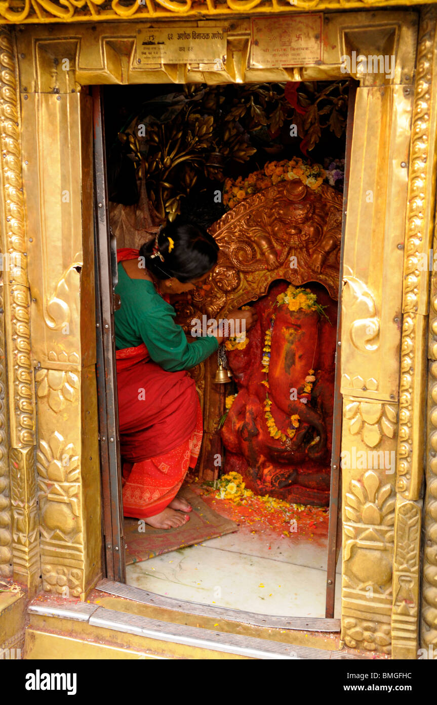 lady praying in small shrine within a hole in the wall temple , road ...