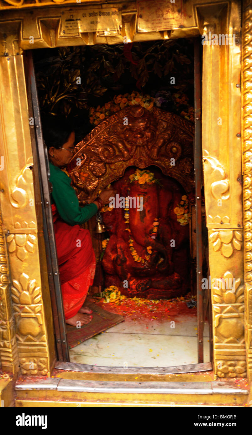 lady praying in small shrine within a hole in the wall temple , road ...