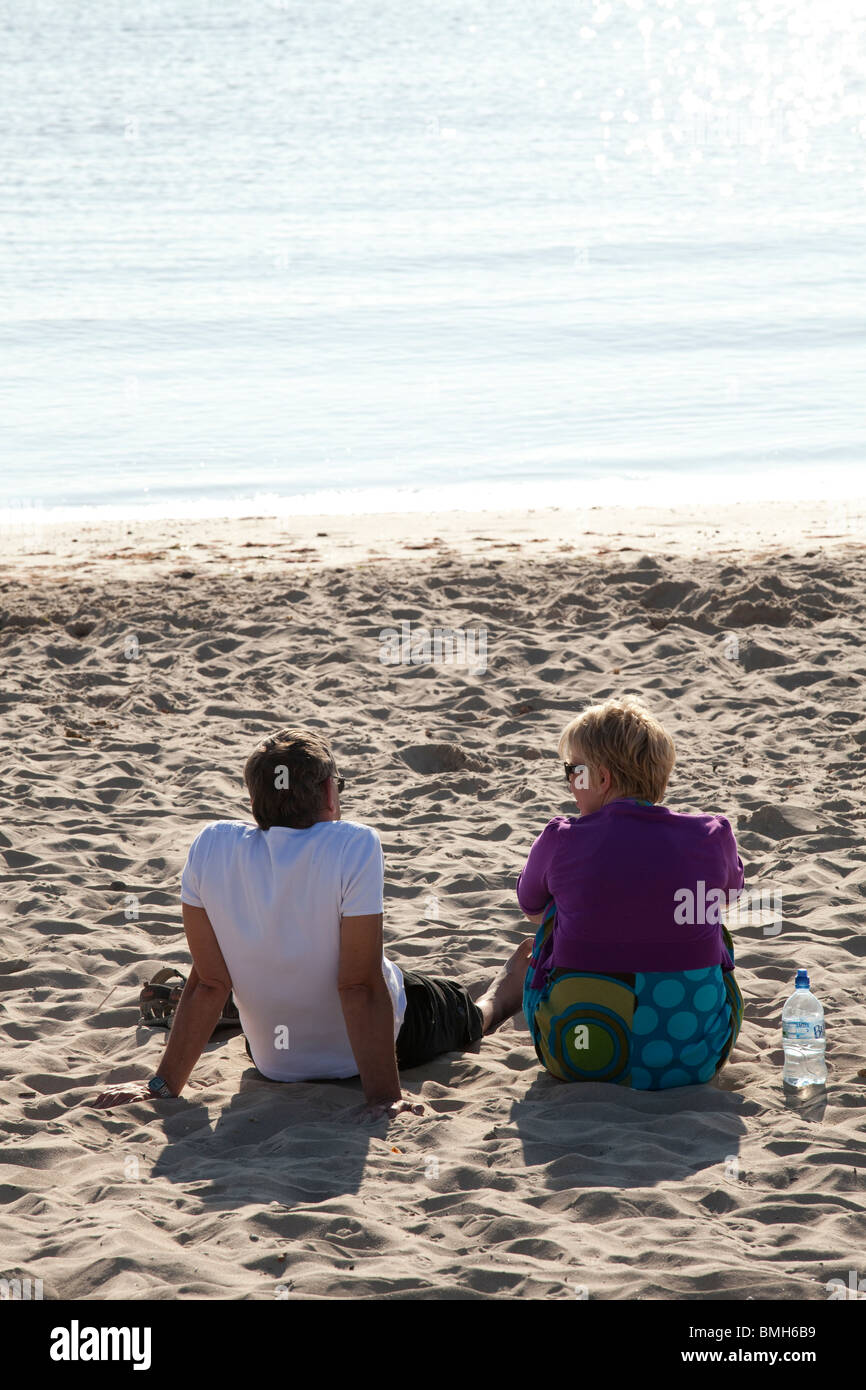 Couple sat alone on sandy beach enjoying early morning sunlight Stock ...