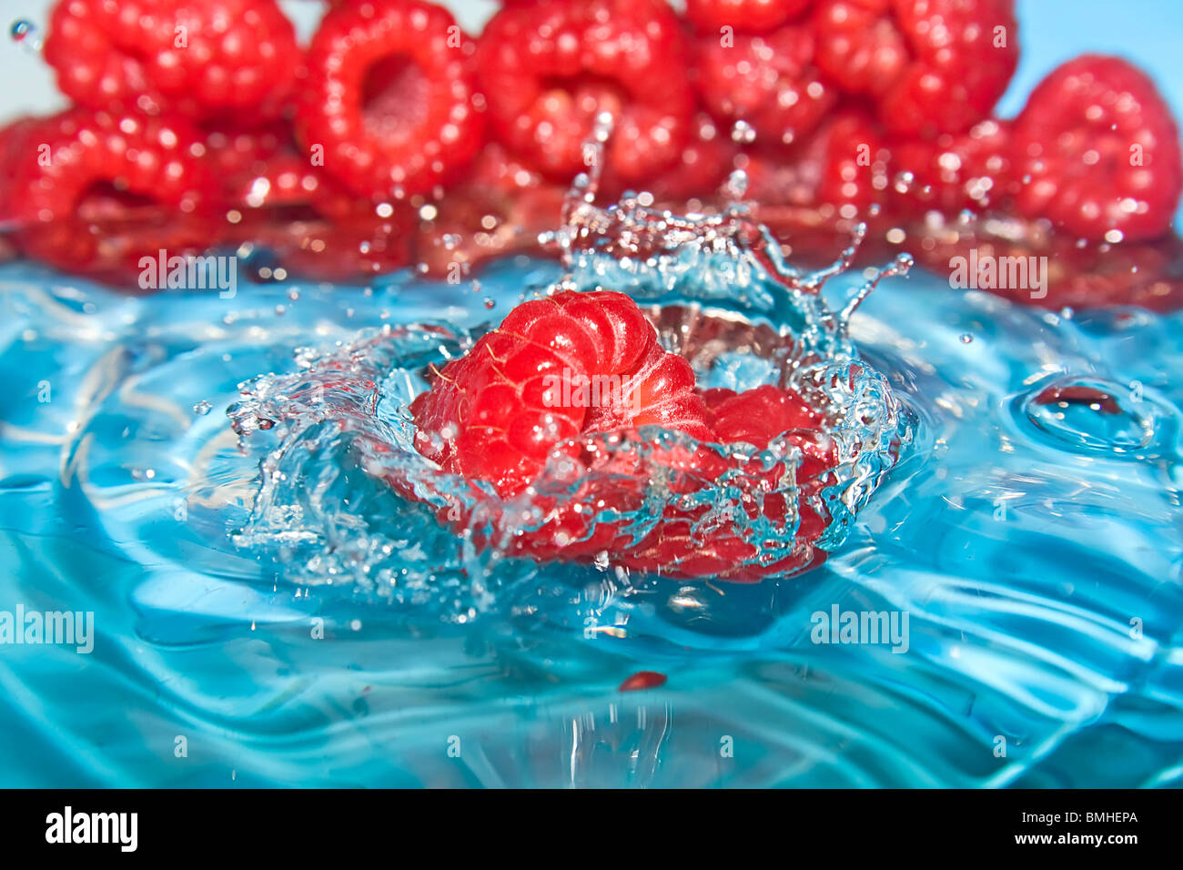 Fresh raspberries dropped to clear, blue water. Splash with fruits ...