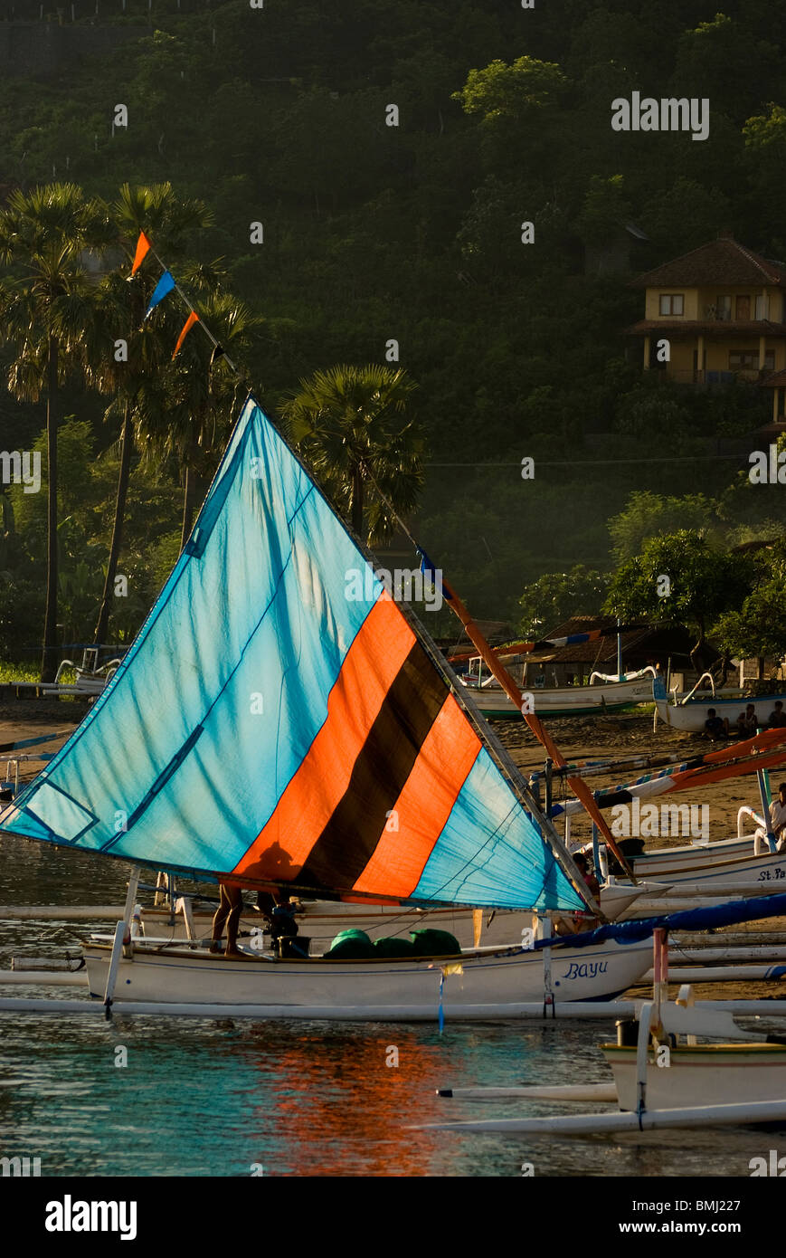 A Balinese outrigger fishing boat, called a jukung, returns to shore in ...