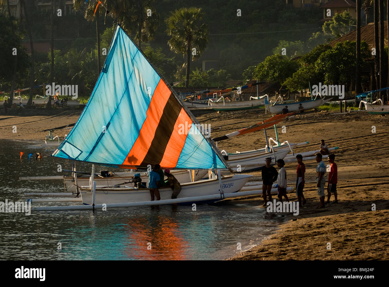 A Balinese outrigger fishing boat, called a jukung, returns to shore in ...