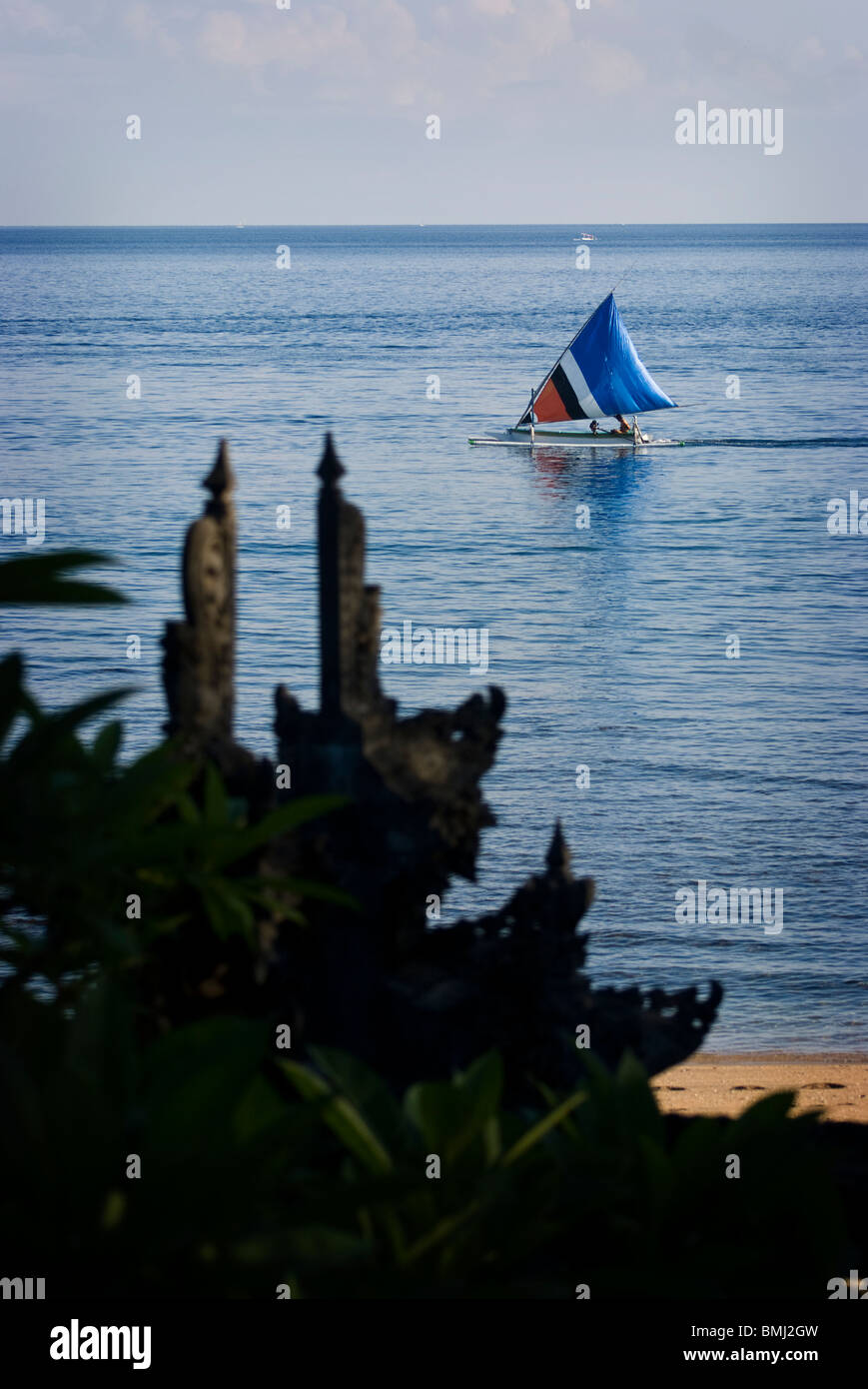 A traditional fishing boat, called a jukung, sails past a small stone ...