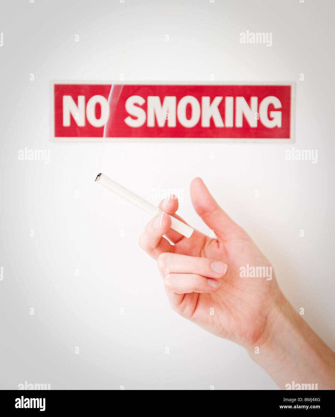 Hand holding cigarette in front of no smoking sign Stock Photo - Alamy