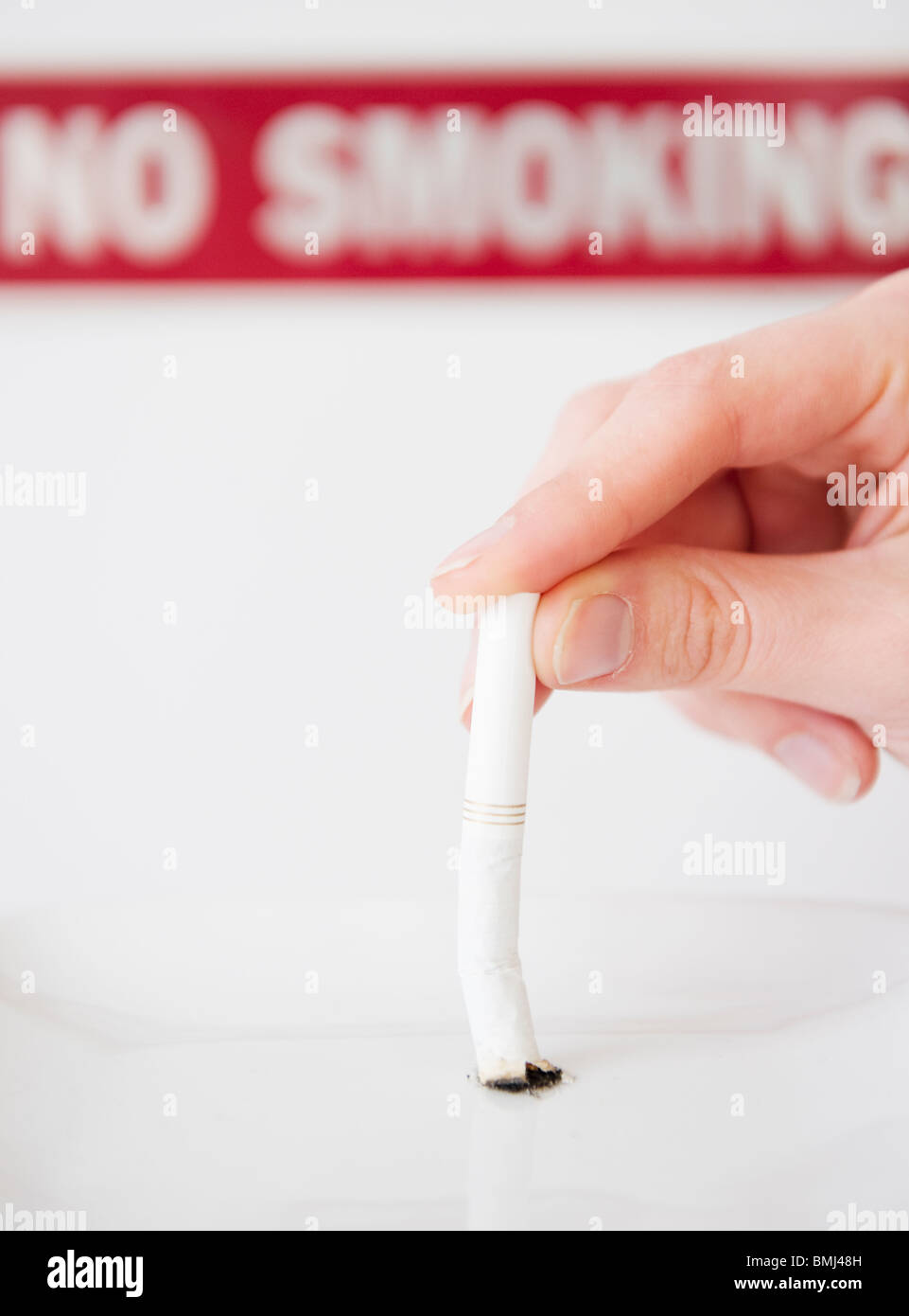 Hand putting out cigarette in front of no smoking sign Stock Photo - Alamy