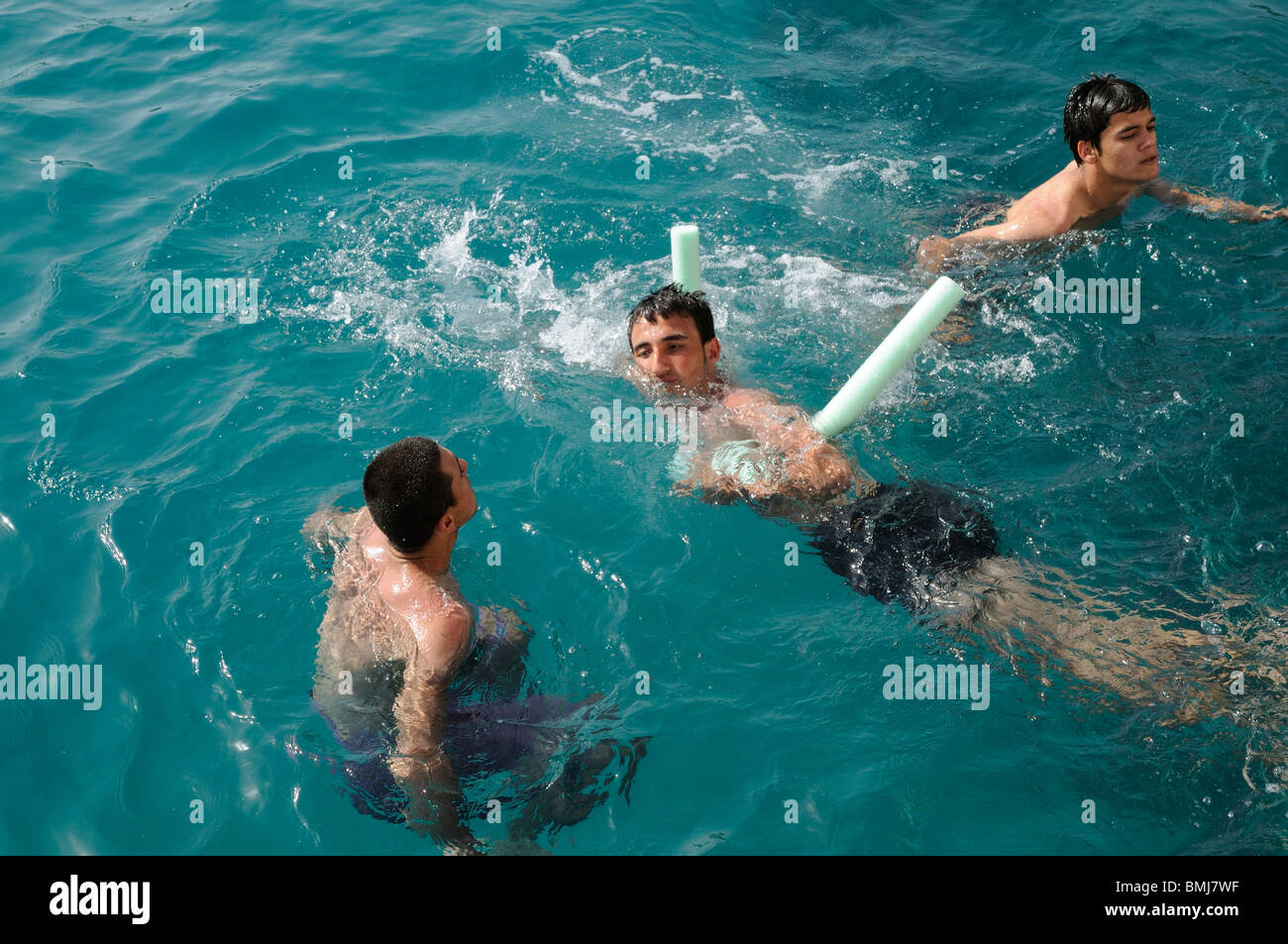 Young man using a swimming noodle as a buoyancy aid as he floats in the ...