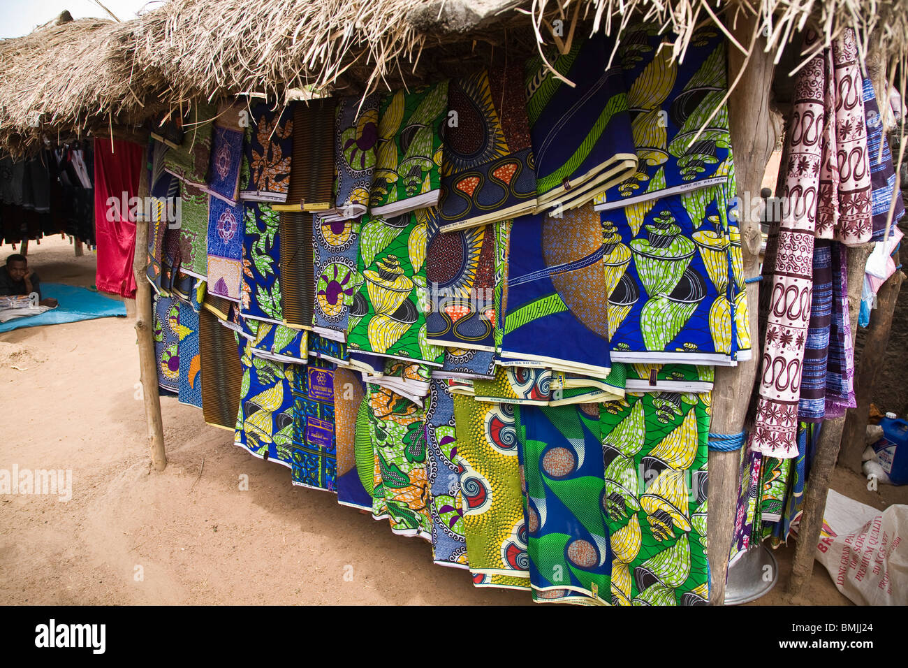 West Africa, Benin. Colorful textiles displayed in thatched structure ...